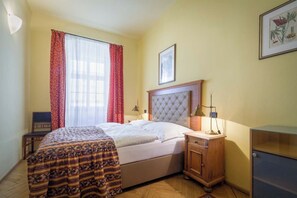 Quarto com cama, mesa de cabeceira, luminária, cadeira e janela com cortinas.