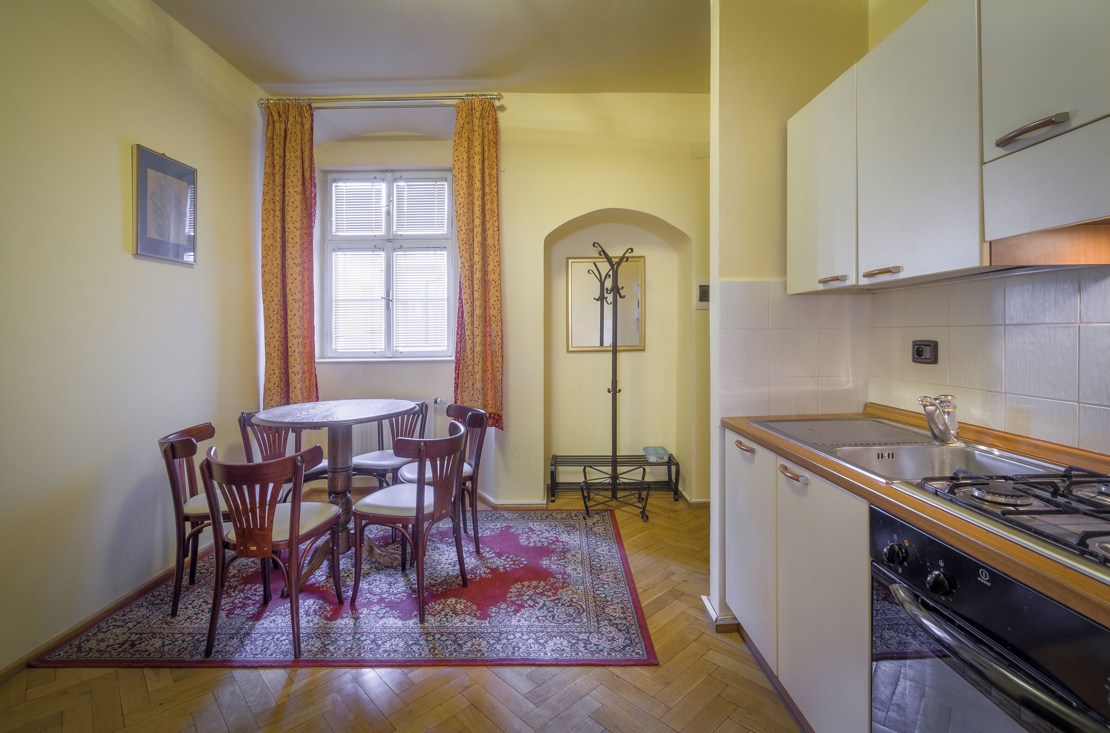 Cozinha compacta com área de refeições, cadeiras de madeira, mesa redonda e tapete.