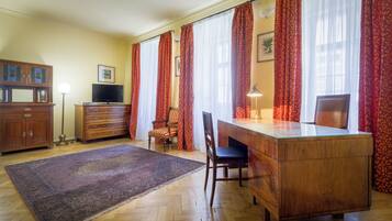 Quarto com escrivaninha de madeira, televisão, cadeira e uma janela grande com cortinas vermelhas.