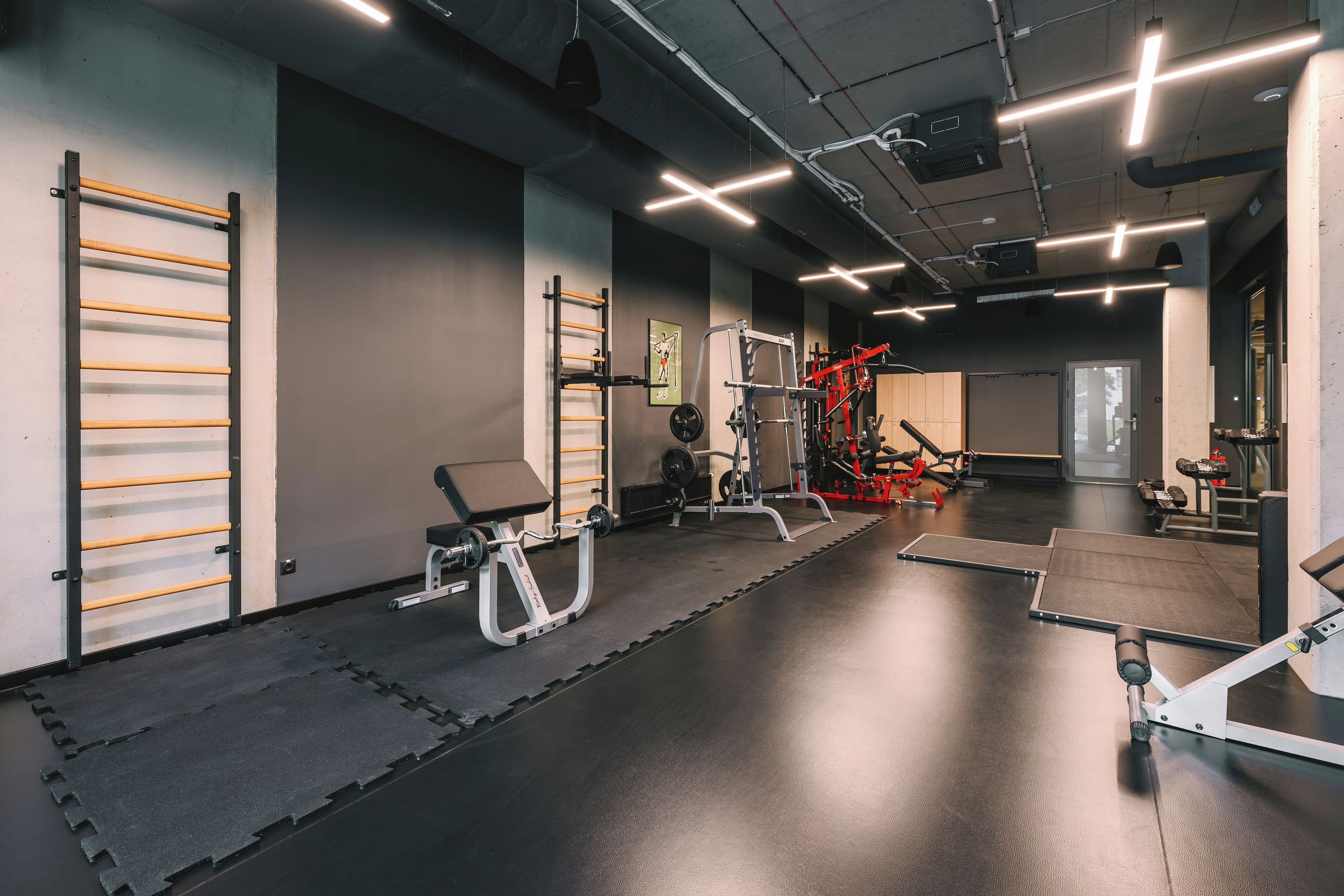 Academia com equipamentos de ginástica, um banco e suporte fixado na parede.