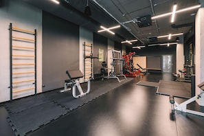 Academia com equipamentos de ginástica, um banco e suporte fixado na parede.