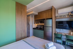 Quarto de hotel compacto com cama, cozinha compacta, escrivaninha e televisão.