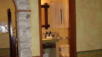 Quarto com arco de pedra que dá para um banheiro, uma cadeira de madeira e uma cama com cobertura azul.