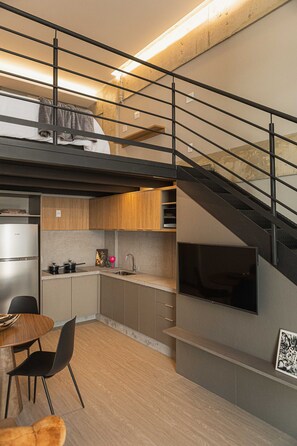 Cozinha moderna com TV integrada, área de refeições com mesa e cadeiras, e escada com corrimão de metal.