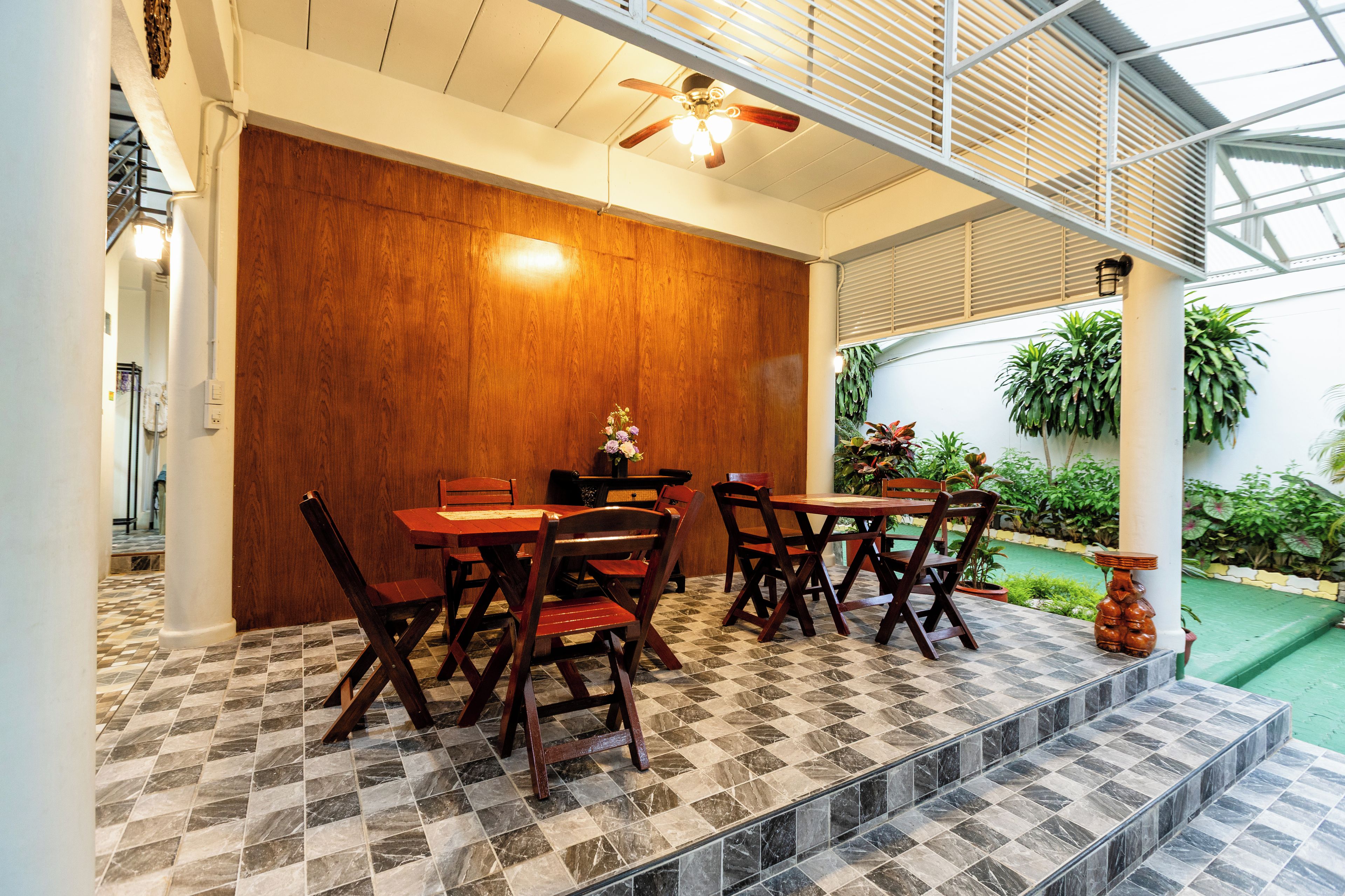 Área de jantar com parede de madeira, ventilador de teto e vista para um jardim.