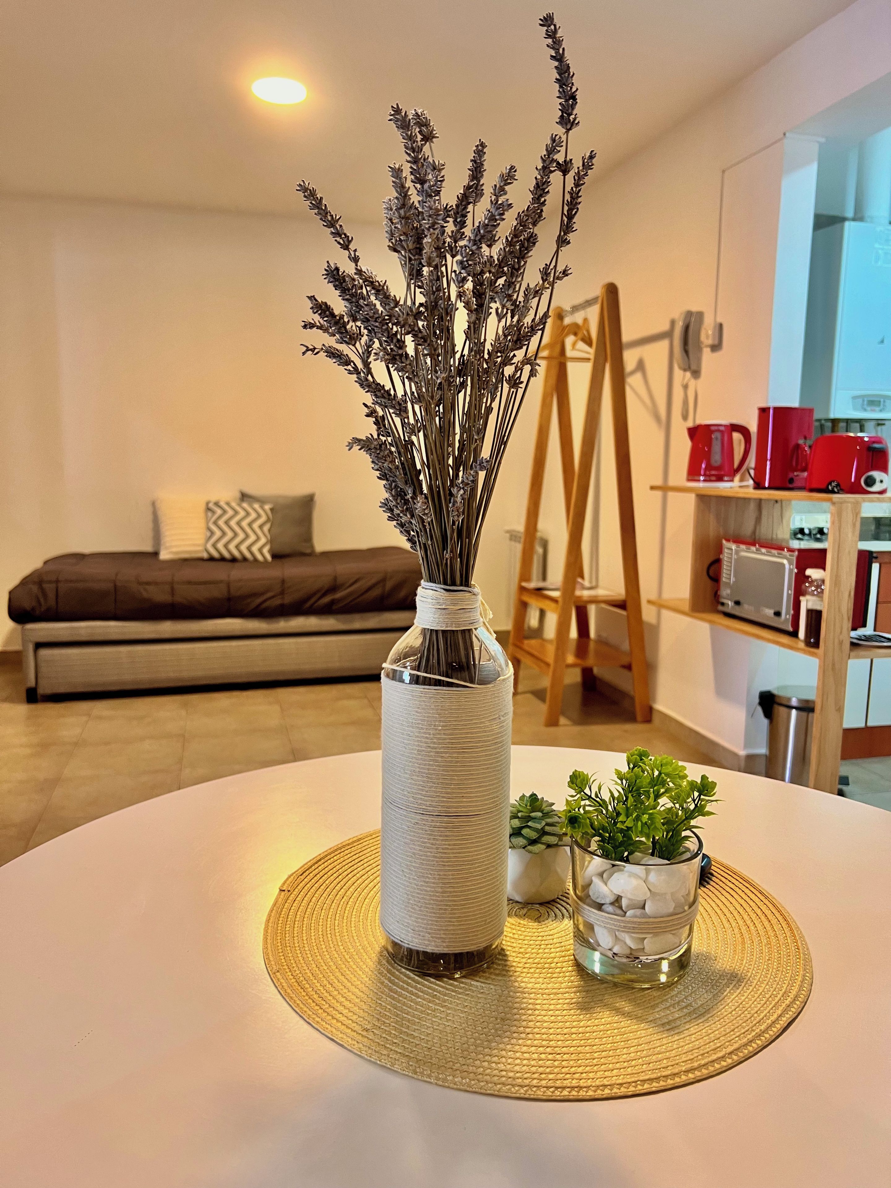 Uma sala de estar com uma mesa redonda, um vaso com lavanda seca, uma pequena planta em vaso e um sofá com almofadas.