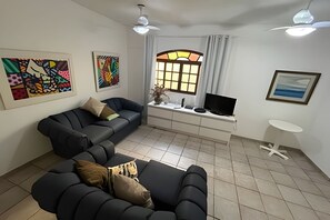 Uma sala de estar com sofá seccional, televisão de tela plana, mesinha e obras de arte nas paredes.