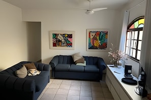Sala de estar com dois sofás, um ventilador de teto e obras de arte nas paredes.