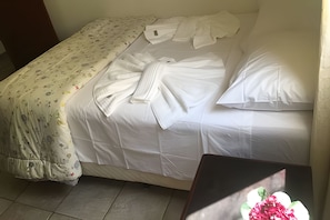 Cama com lençóis brancos e manta com padrão floral.