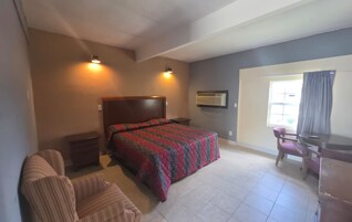Quarto com cama, escrivaninha, cadeira e janela.