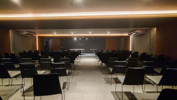 Uma sala de conferências com fileiras de cadeiras e mesas, um pódio e um palco na frente.