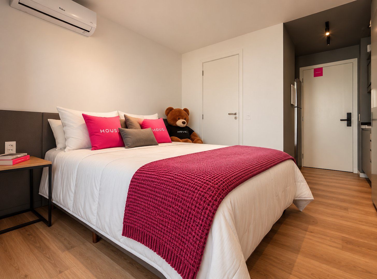 Quarto de hotel com uma cama, um urso de pelúcia e um cobertor vermelho.