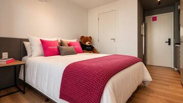 Quarto de hotel com uma cama, um urso de pelúcia e um cobertor vermelho.
