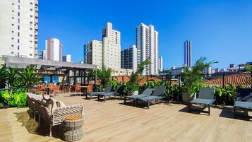 Terraço no telhado com cadeiras de descanso, área de bar e vista para edifícios altos.