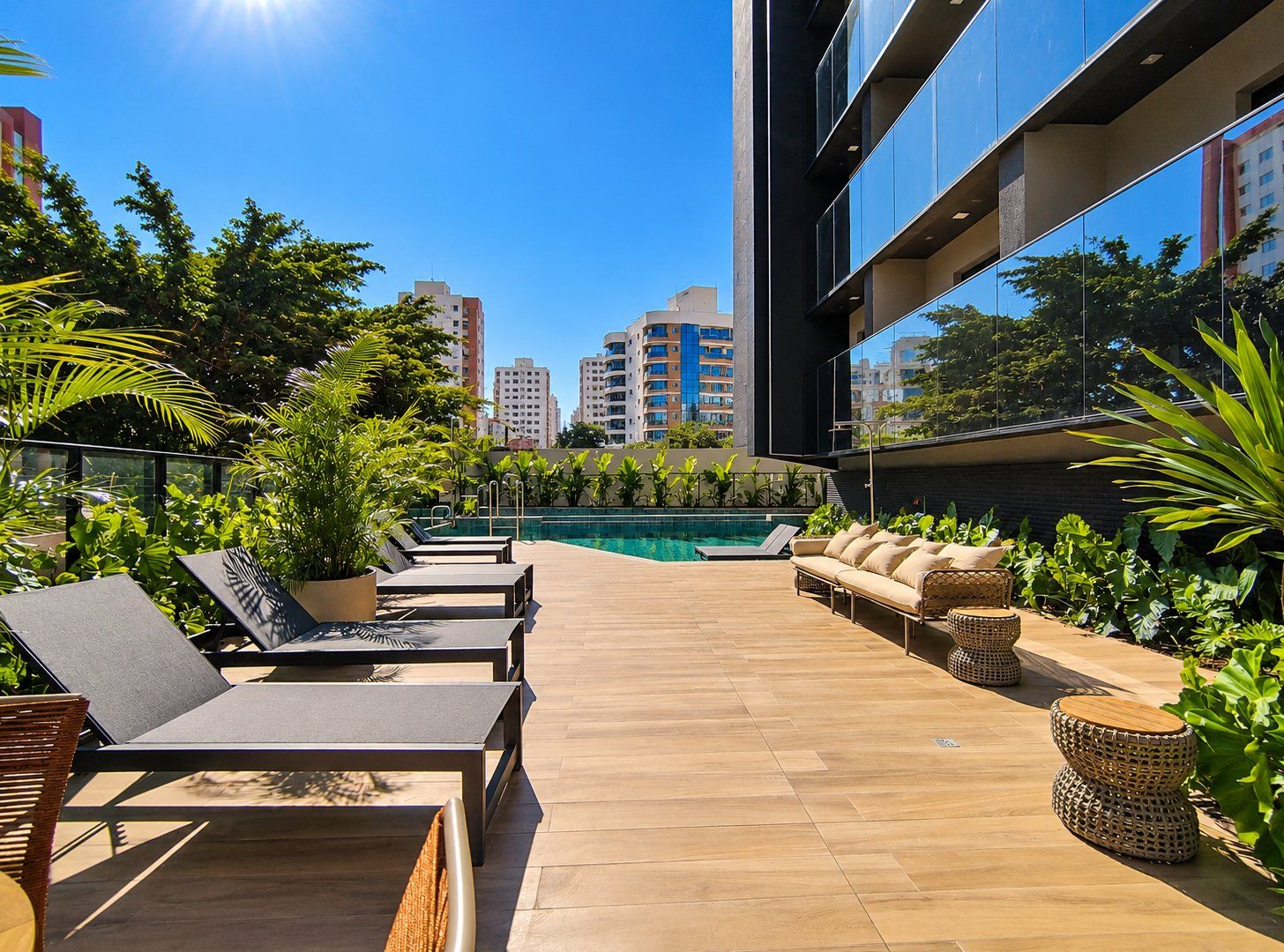 Área de piscina no terraço com espreguiçadeiras, espaço para sentar e vista dos edifícios ao redor.