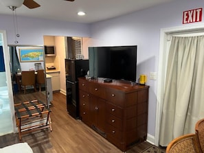 Quarto de hotel com cômoda de madeira, televisão de tela plana, área de refeições com cadeiras e placa de saída.