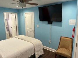 Quarto com cama, cadeira, televisão na parede e ventilador de teto.