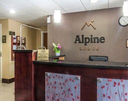 Bancada de recepção no Alpine Lodge, com um relógio, um aviso sobre programa de recompensas e um vaso de flores.