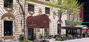Um edifício histórico com uma entrada imponente identificada como 'The Tremont Hotel' e toldo vermelho.