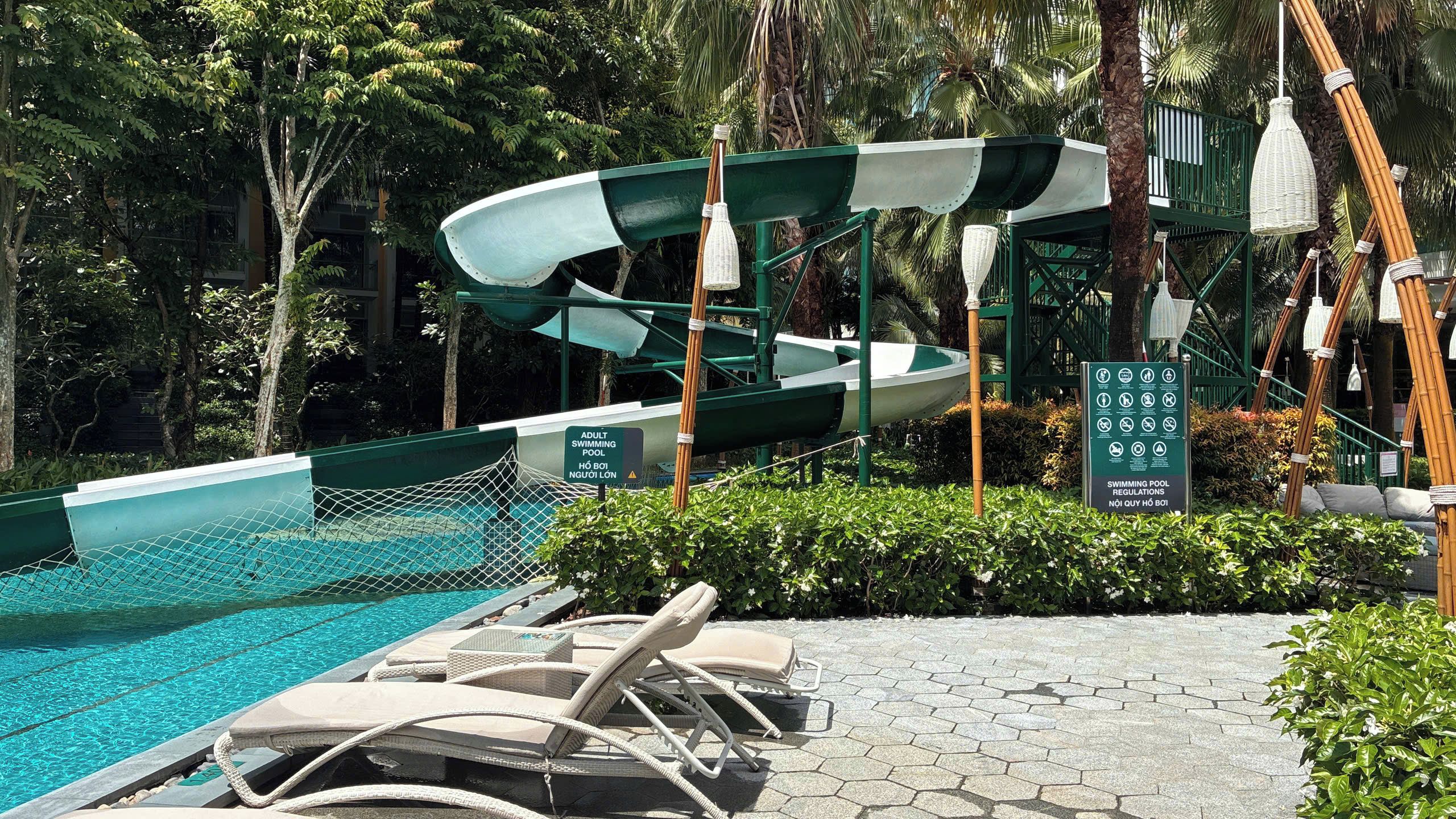 Área de piscina com escorregador, espreguiçadeiras e placa com as regras da piscina para adultos.