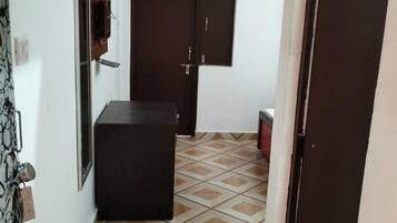 Quarto com piso de azulejos, um armário escuro, uma porta e uma luminária fixada na parede.