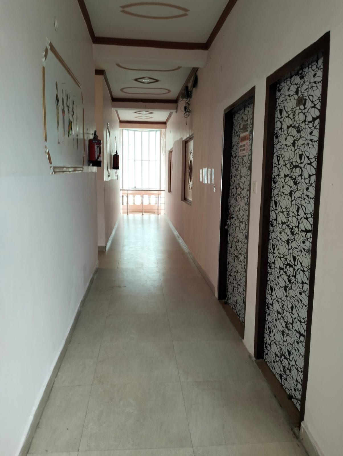 Um corredor com piso ladrilhado, obras de arte emolduradas nas paredes e uma porta com padrão decorativo.