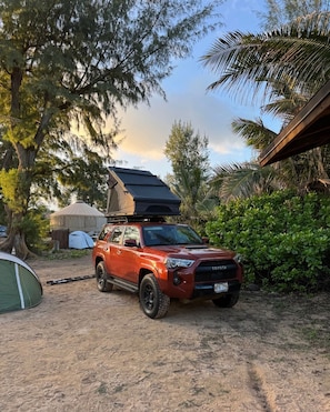 Um SUV vermelho estacionado em um camping com uma barraca e uma cobertura.