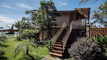 Um imóvel residencial com escada de madeira que dá para uma varanda, cercado por vegetação exuberante e uma piscina.