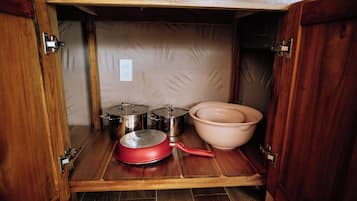 Um armário de madeira com uma prateleira contendo utensílios de cozinha, incluindo panelas, frigideiras e um escorredor.