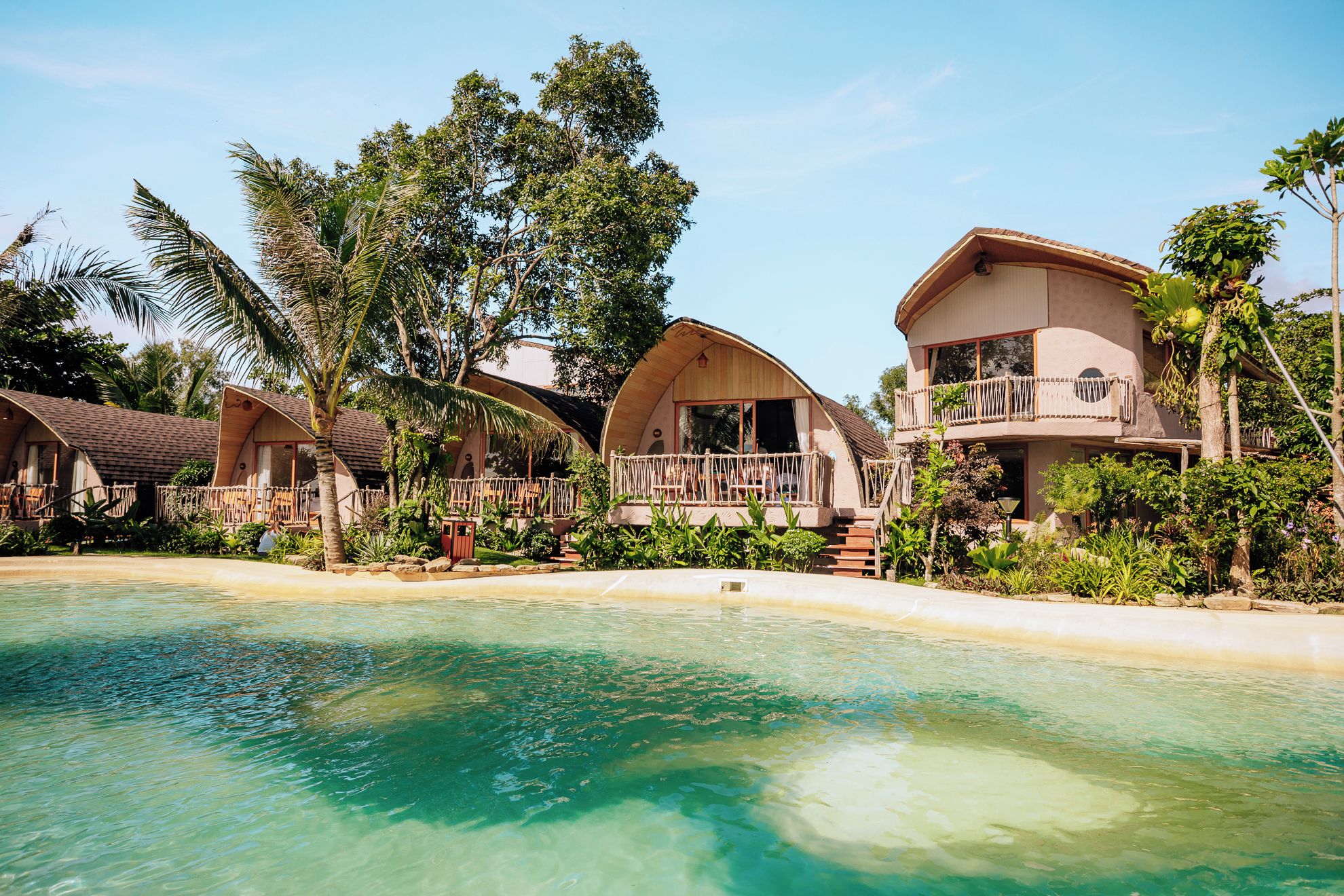 Um resort com várias acomodações no estilo de bangalô, piscina e vegetação tropical exuberante.