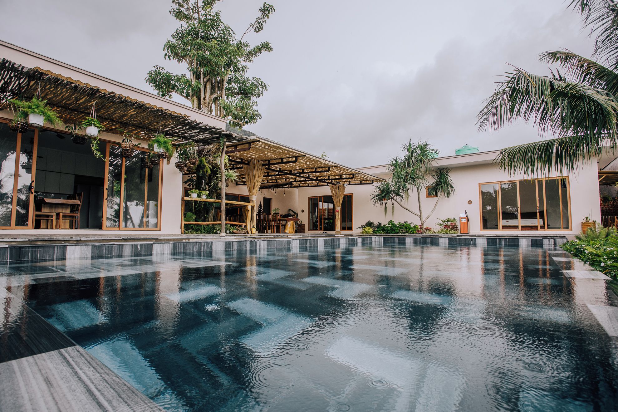 Uma área de piscina moderna com superfície de água cristalina, rodeada por vegetação exuberante e um espaço de estar coberto.
