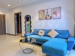 Uma sala de estar moderna com um sofá azul, almofadas decorativas, uma mesa de centro de vidro e obras de arte na parede, incluindo a Torre Eiffel.