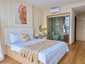 Quarto de hotel com cama, mesa de cabeceira, luminária, espelho, janela e guarda-roupa.