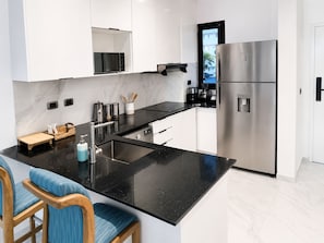 Cozinha moderna com bancada preta, eletrodomésticos de aço inoxidável e painel de vidro marmorizado.