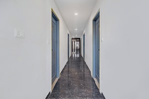 Um corredor comprido e estreito, com chão de mármore escuro e portas azuis de ambos os lados.