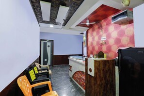Uma área de recepção com balcão, geladeira preta e ventilador de teto.