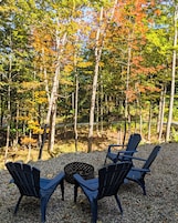 Área arborizada com lareira e quatro cadeiras Adirondack.