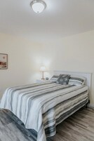 Quarto com cama, mesa de cabeceira com abajur e quadro na parede.