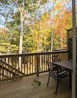 Um deck de madeira com mesa e cadeiras, com vista para uma floresta com folhagem outonal.
