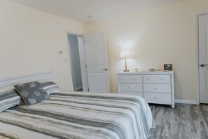 Quarto com cama, mesa de cabeceira, abajur e porta.