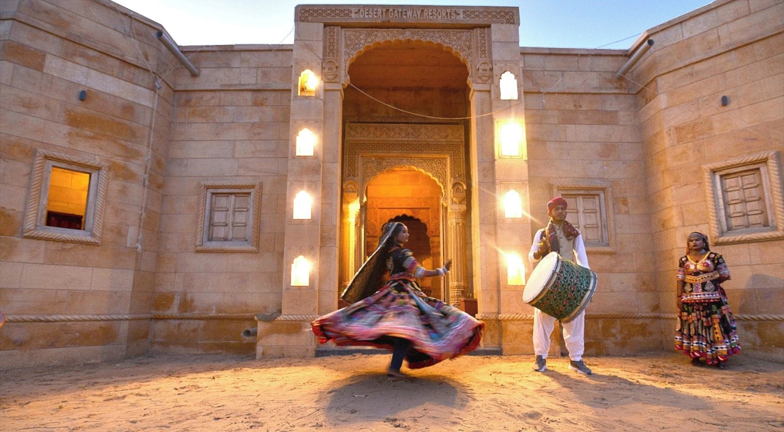 Um edifício histórico com uma entrada ornamentada, uma pessoa tocando tambor e outra vestida com traje típico.