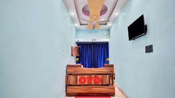 Uma área de recepção com balcão de madeira identificado com 'OYO', ventilador de teto, TV de tela plana e cortina azul.
