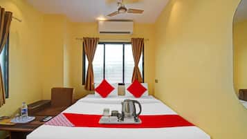 Quarto de hotel com uma cama, escrivaninha, garrafa de água, chaleira e telefone.
