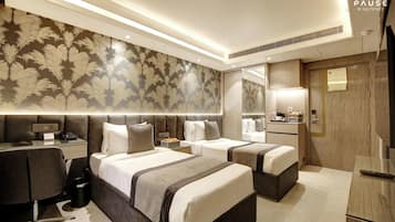 Quarto de hotel com duas camas, uma escrivaninha, uma cadeira, um cesto de lixo e um espelho.