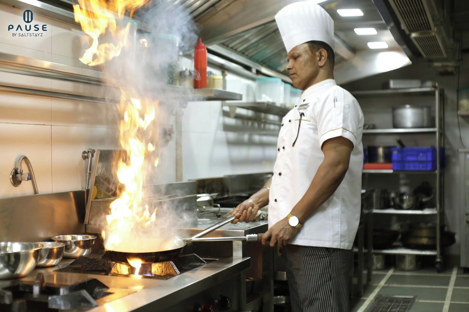 Um chef cozinhando com chamas em um fogão em uma cozinha profissional.
