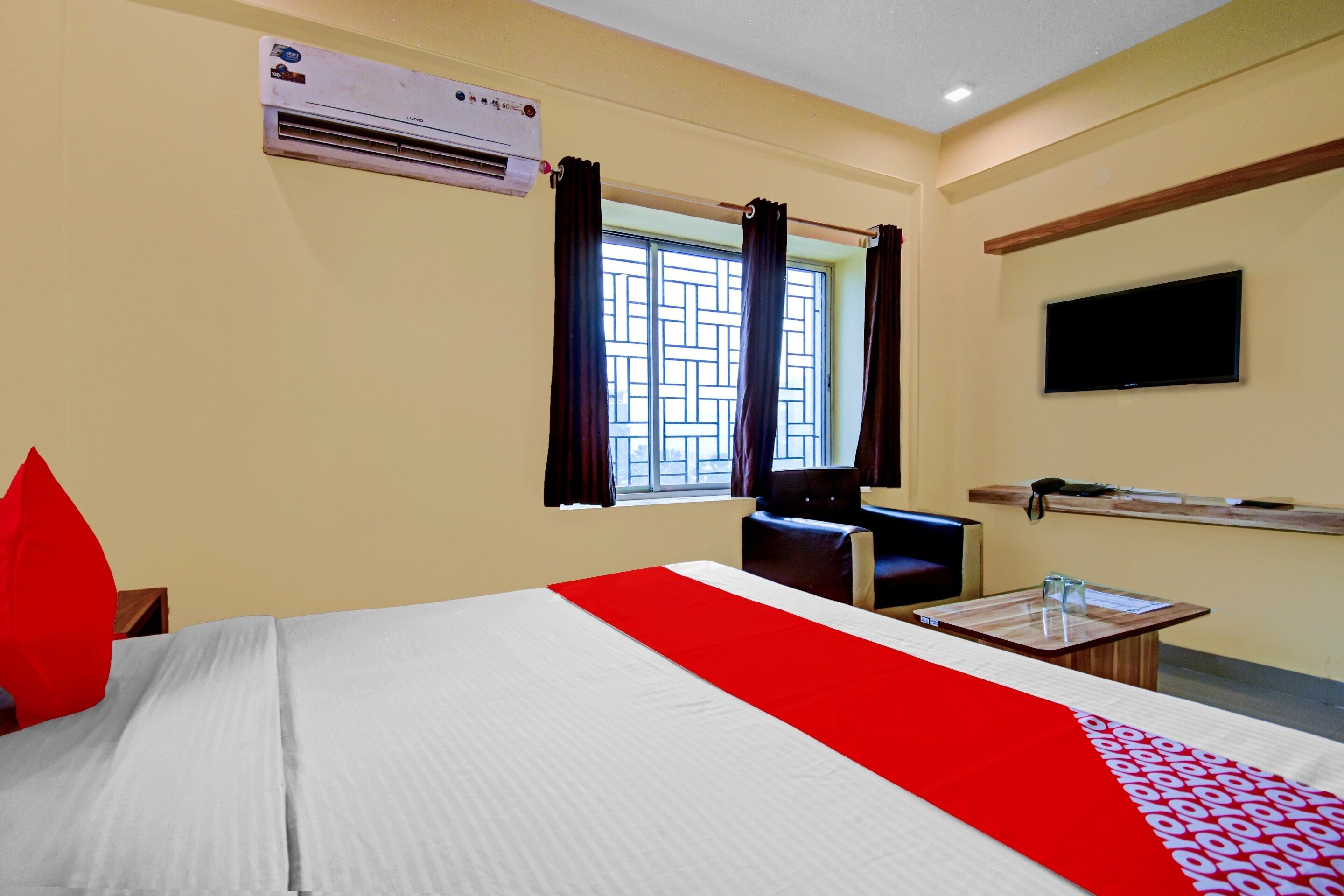 Quarto de hotel com cama, televisão, janela com cortinas e ar condicionado.