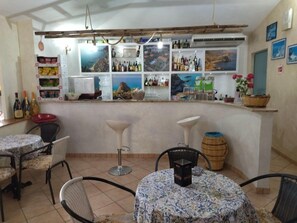 Uma área de bar com balcão, prateleiras cheias de garrafas e dois bancos.