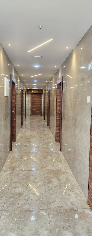 Corredor com piso de mármore, portas de madeira e iluminação embutida.
