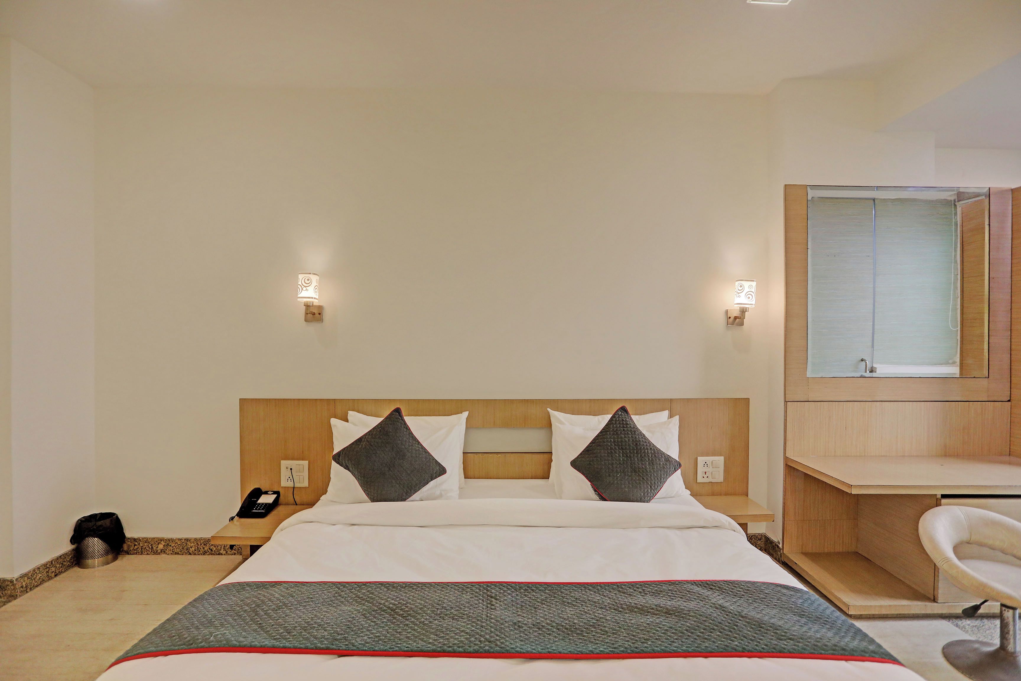 Quarto de hotel com cama, mesa de cabeceira, luminária e espelho.