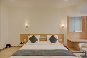 Quarto de hotel com cama, mesa de cabeceira, luminária e espelho.